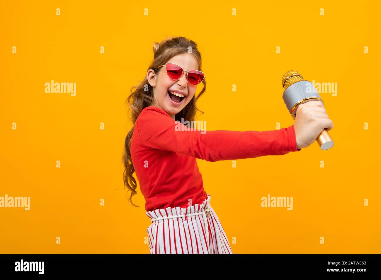 young singer with a microphone in her hands on a yellow studio ...