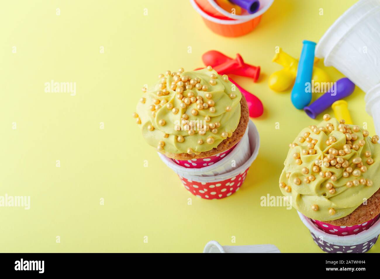 Funny cupcakes in funny polka dot cups and deflated balloons on yellow ...