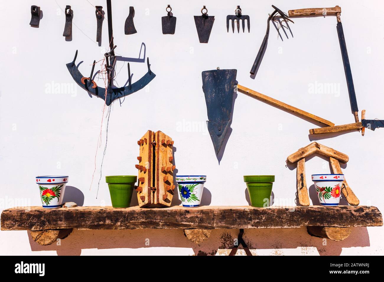 Old farm tools and colorful decorated terracotta pots, on a white wall ...
