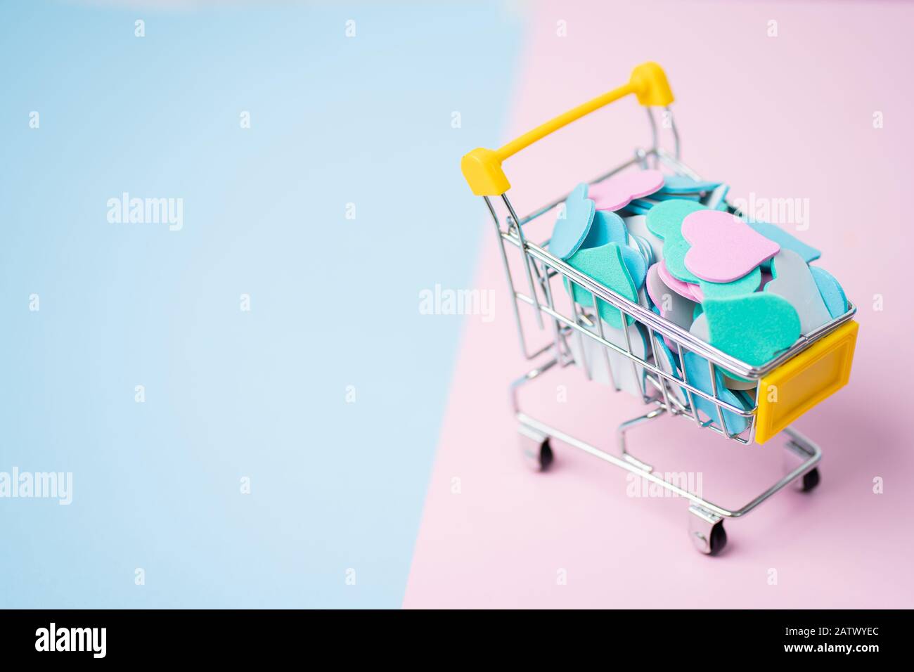 Closeup of a miniature cart full of colorful hearts on a two tone pink ...