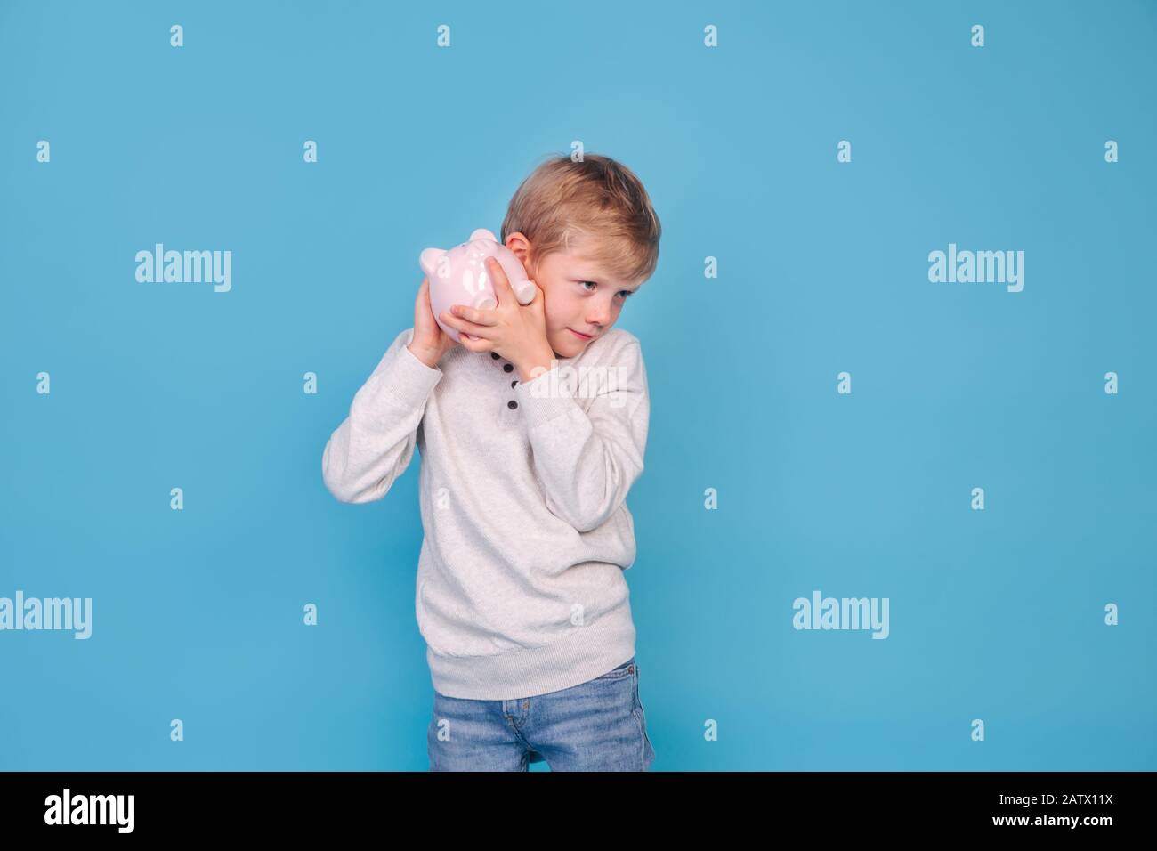 Cute little boy shaking piggy box on blue background Stock Photo - Alamy