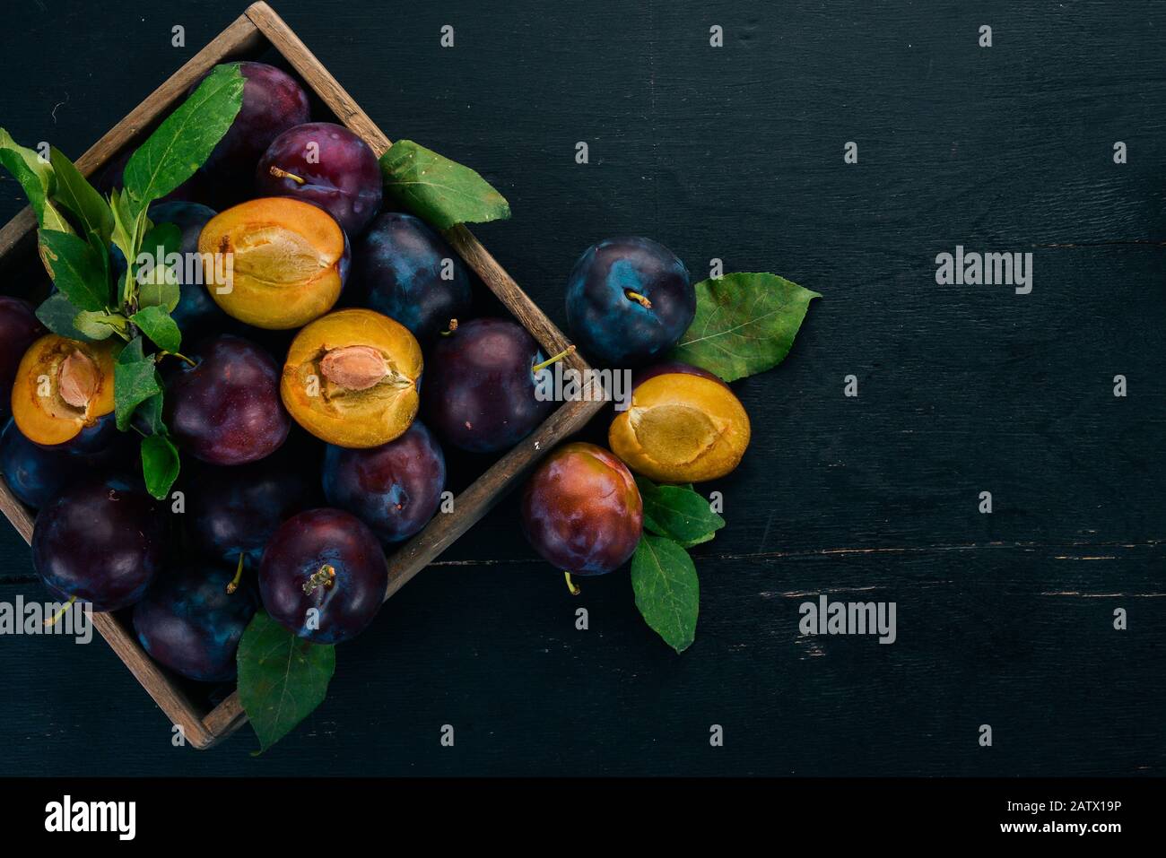 Plums with leaves in a wooden box. On a black wooden background. Top ...
