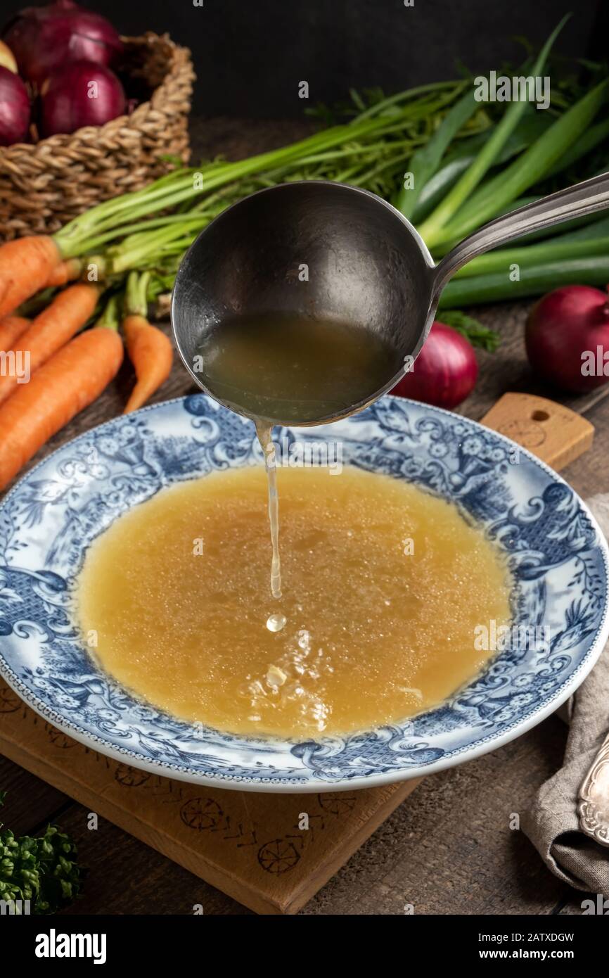 Pouring chicken bone broth into a vintage plate with a ladle Stock ...