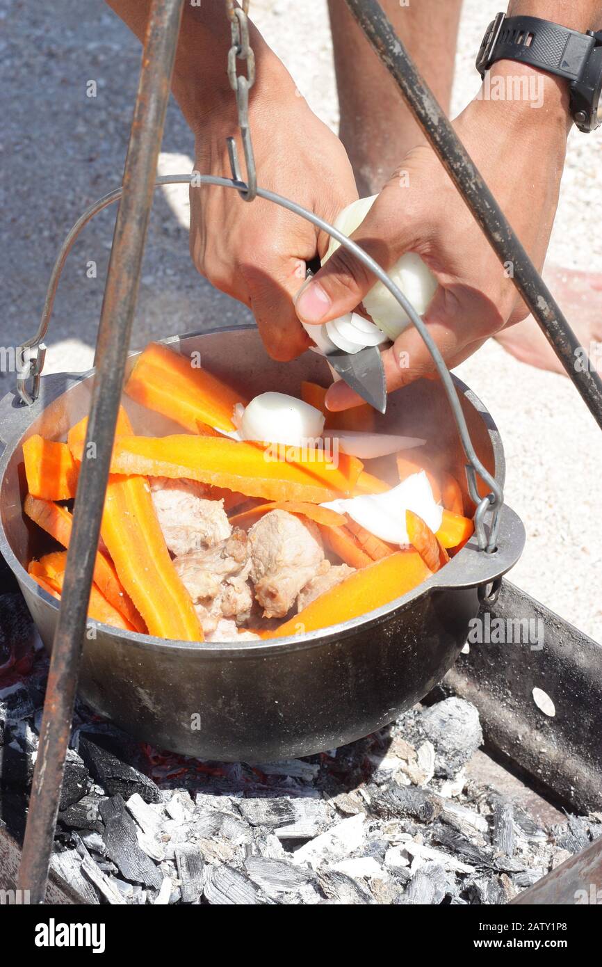 Tourist cooking meat with vegetables in a cauldron on the beach. Summer ...