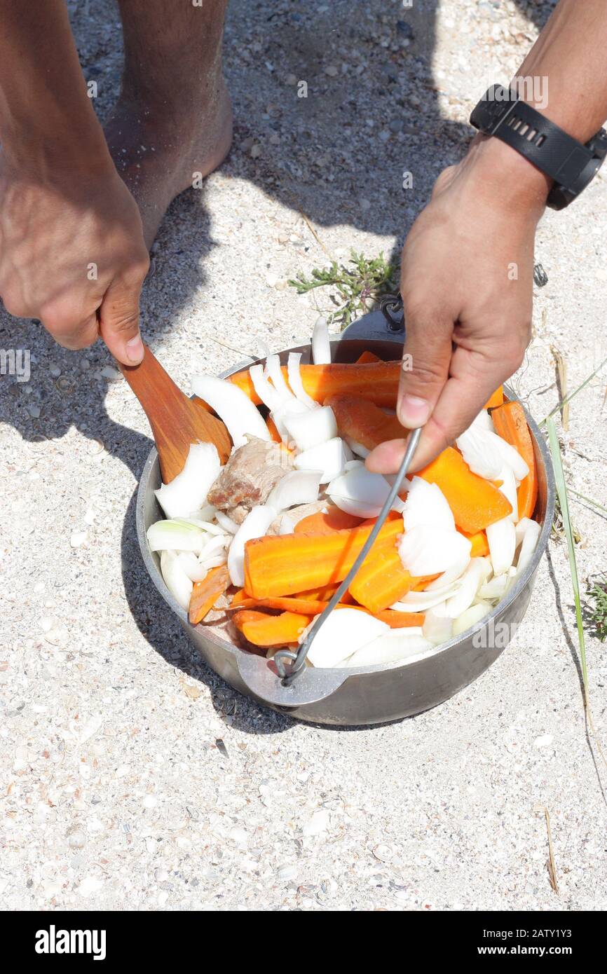 Tourist cooking meat with vegetables in a cauldron on the beach. Summer ...