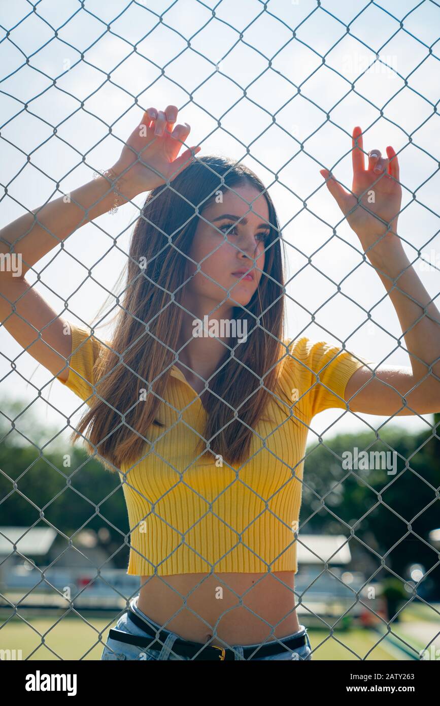 Teenage girl in yellow top standing with arms raised behind chain link ...