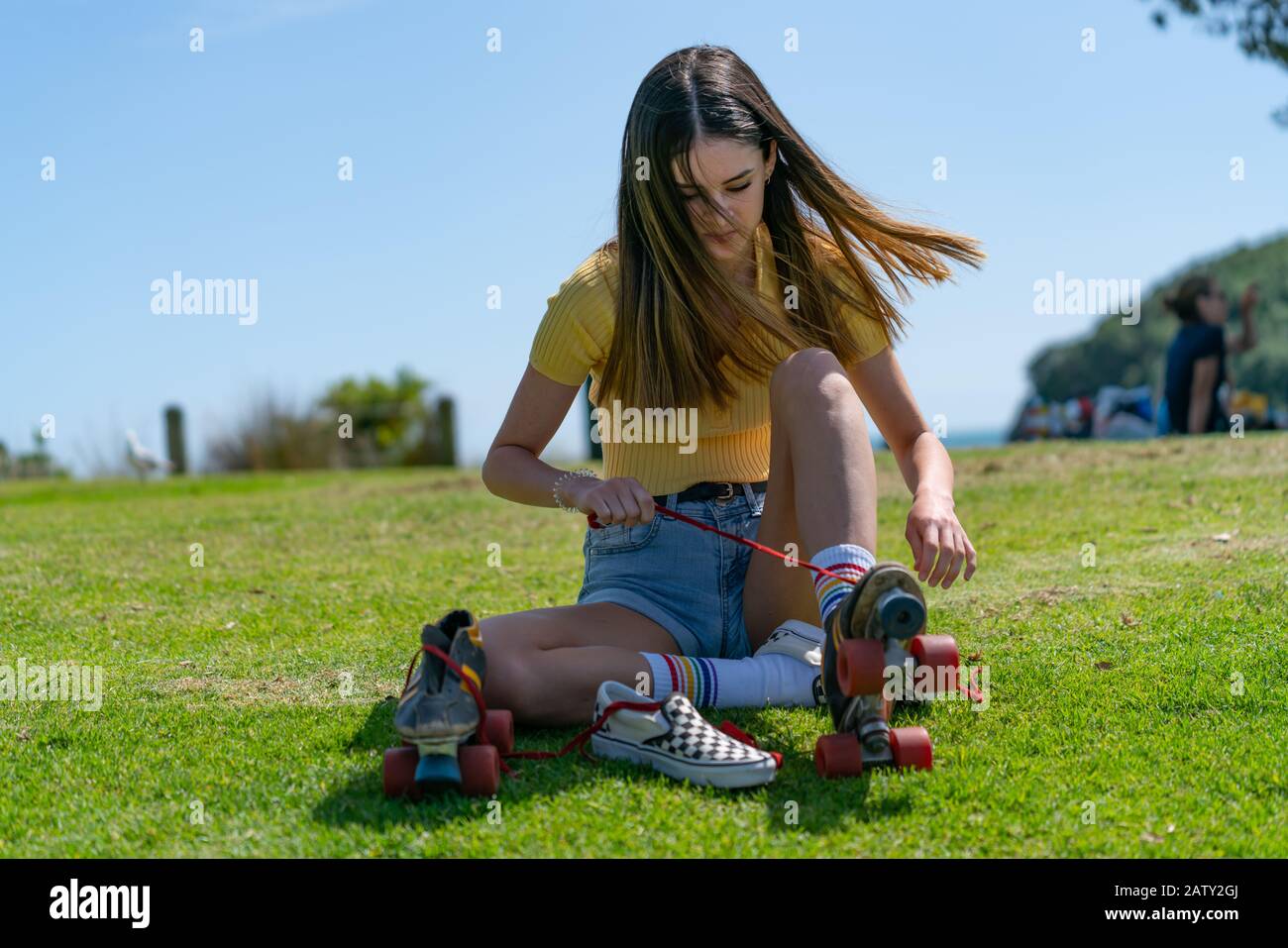 Pretty teenage girl in yellow top sits on grass putting retro style ...