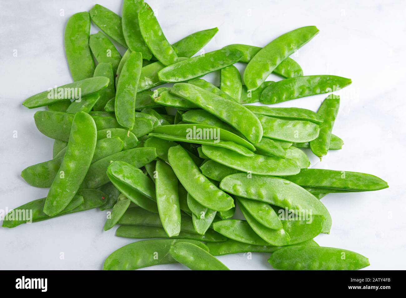 Overhead view of fresh raw sugar snap peas on a light marbled surface ...
