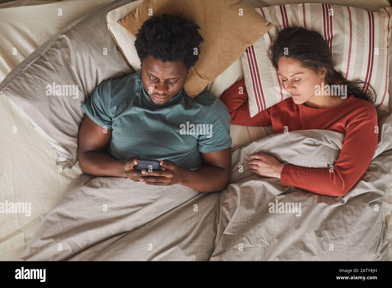 High angle view of African young man lying in bed and using his mobile ...