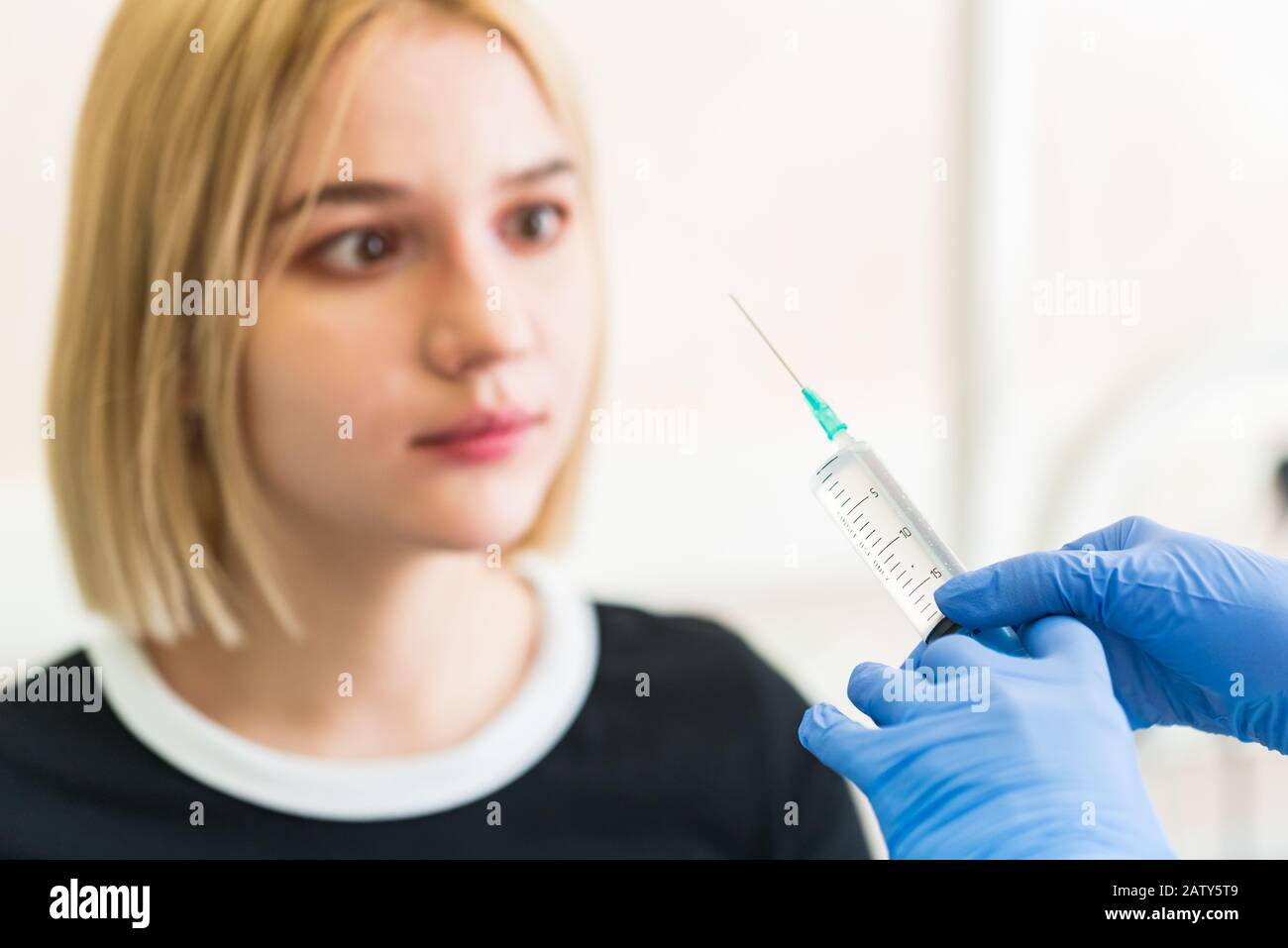 Fear of injections. Frightened girl looks at syringe needle during ...
