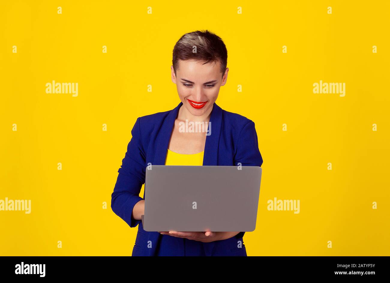 Smiling woman sending emails on her laptop computer isolated yellow ...