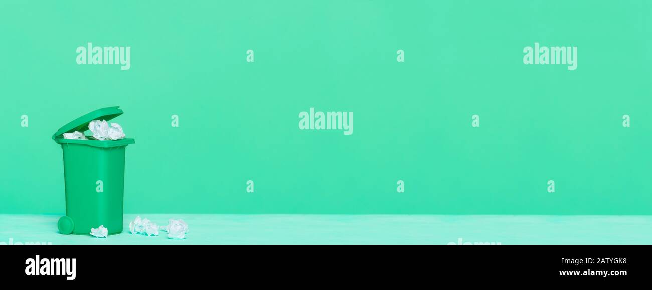 A green plastic garbage bin and paper on green background, great for ...