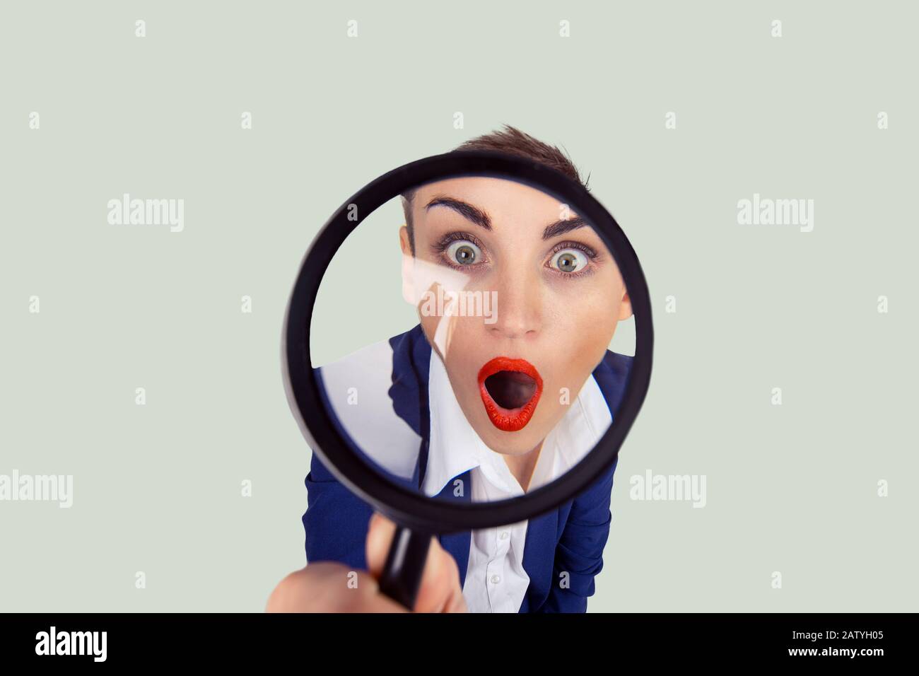 Amazed surprised woman looking through a magnifying glass over light ...