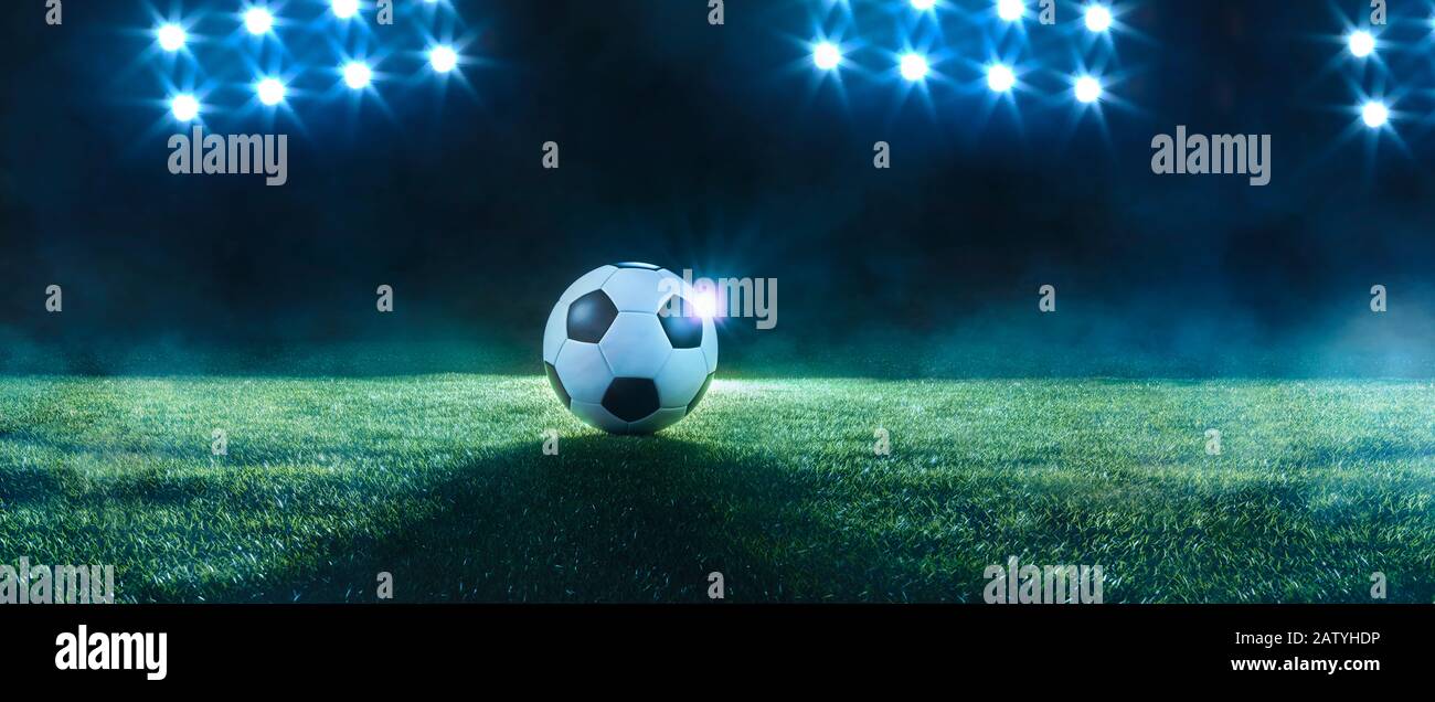 Soccer ball on a football field backlit by two banks of eight bright ...