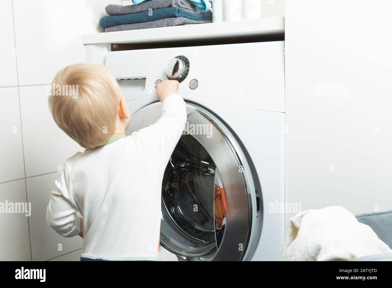 Two year old child doing household chores. Loading washing machine ...