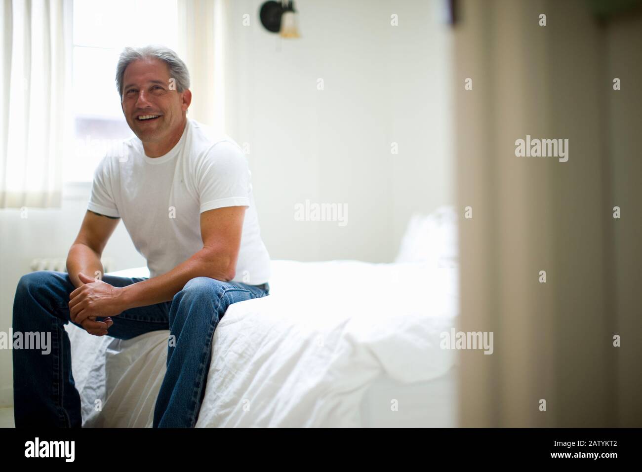 Happy Mature Man Sitting On The Edge Of The Bed In His Bedroom Stock