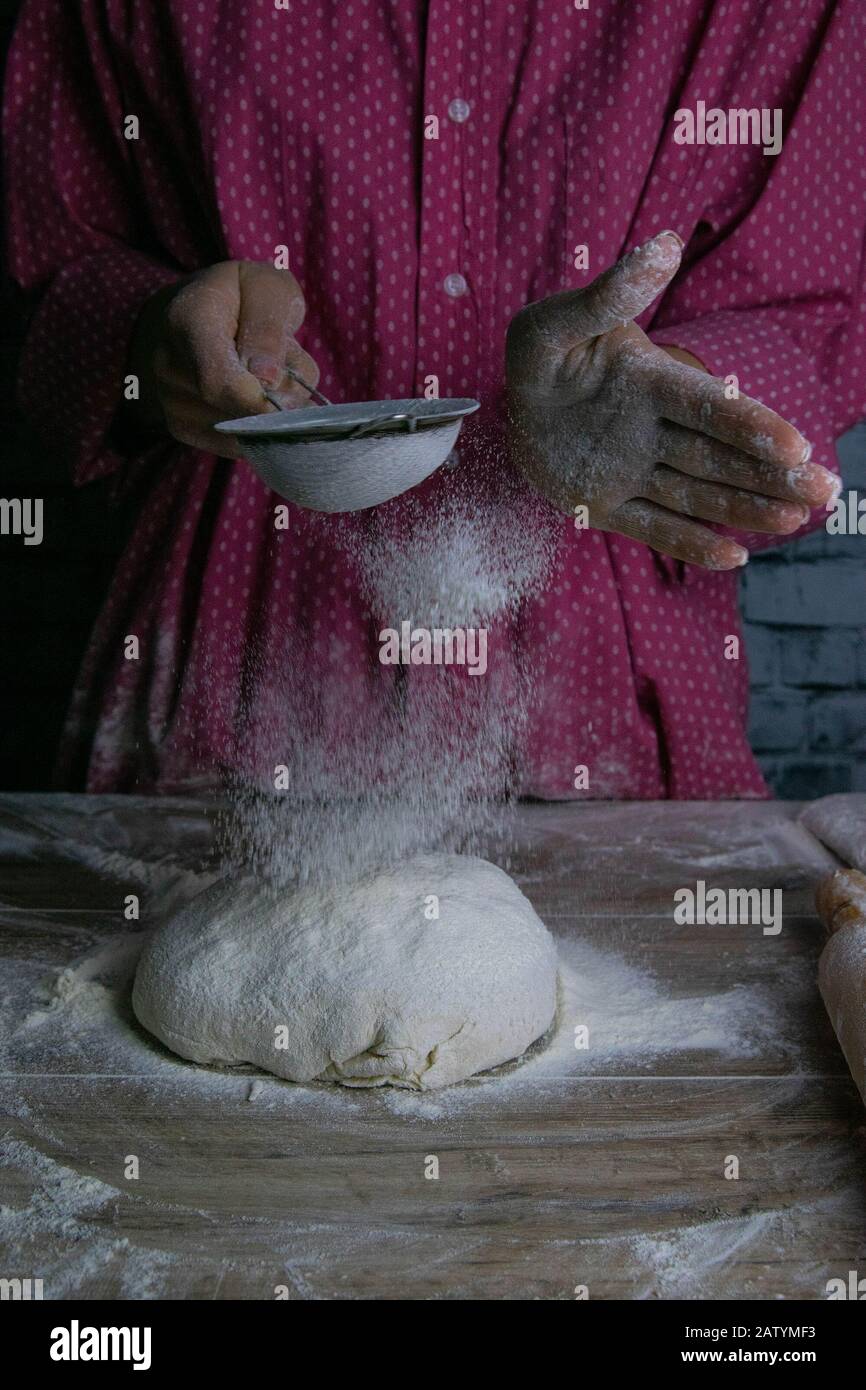 The woman sprinkles flour dough from the fullness for sifting flour ...
