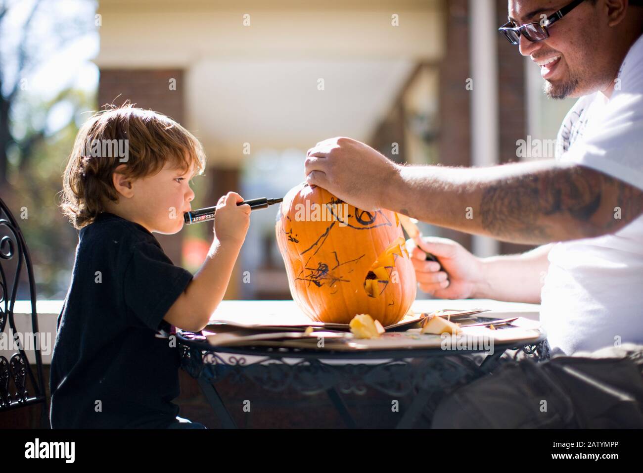 Father and son drawing face on pumpkin and carving Jack O' Lantern ...