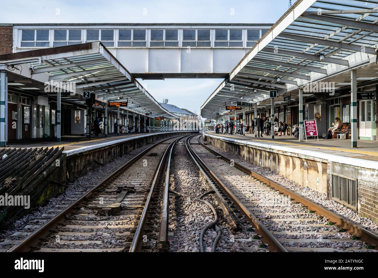 Passengers awaiting a train to arrive at a train station standing on ...