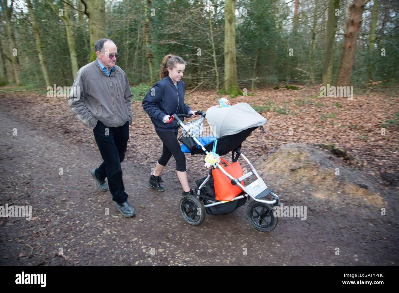 A teenage mum pushing her baby in a buggy while walking with her father ...