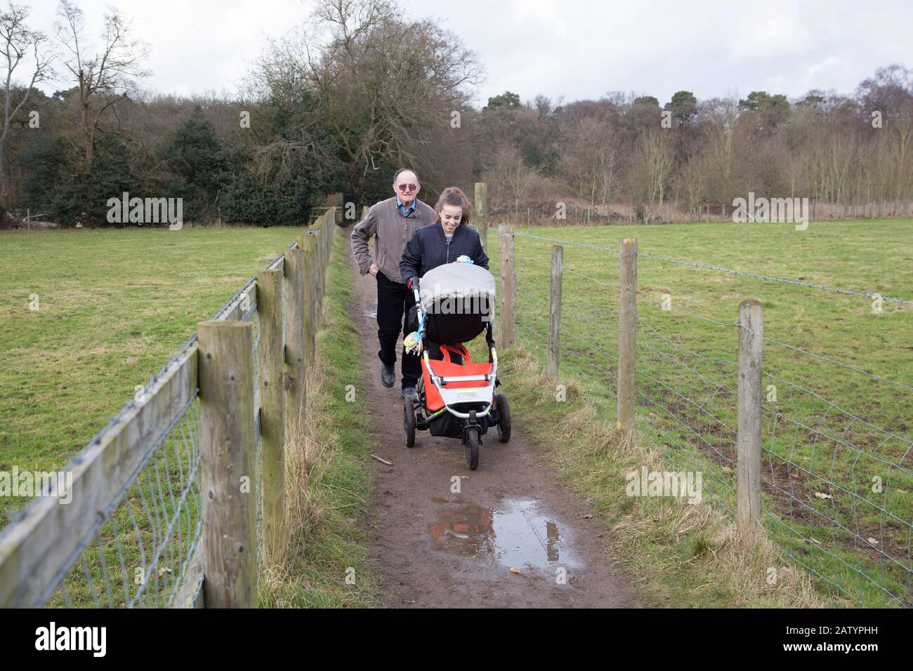 A teenage mum pushing her baby in a buggy while walking with her father ...