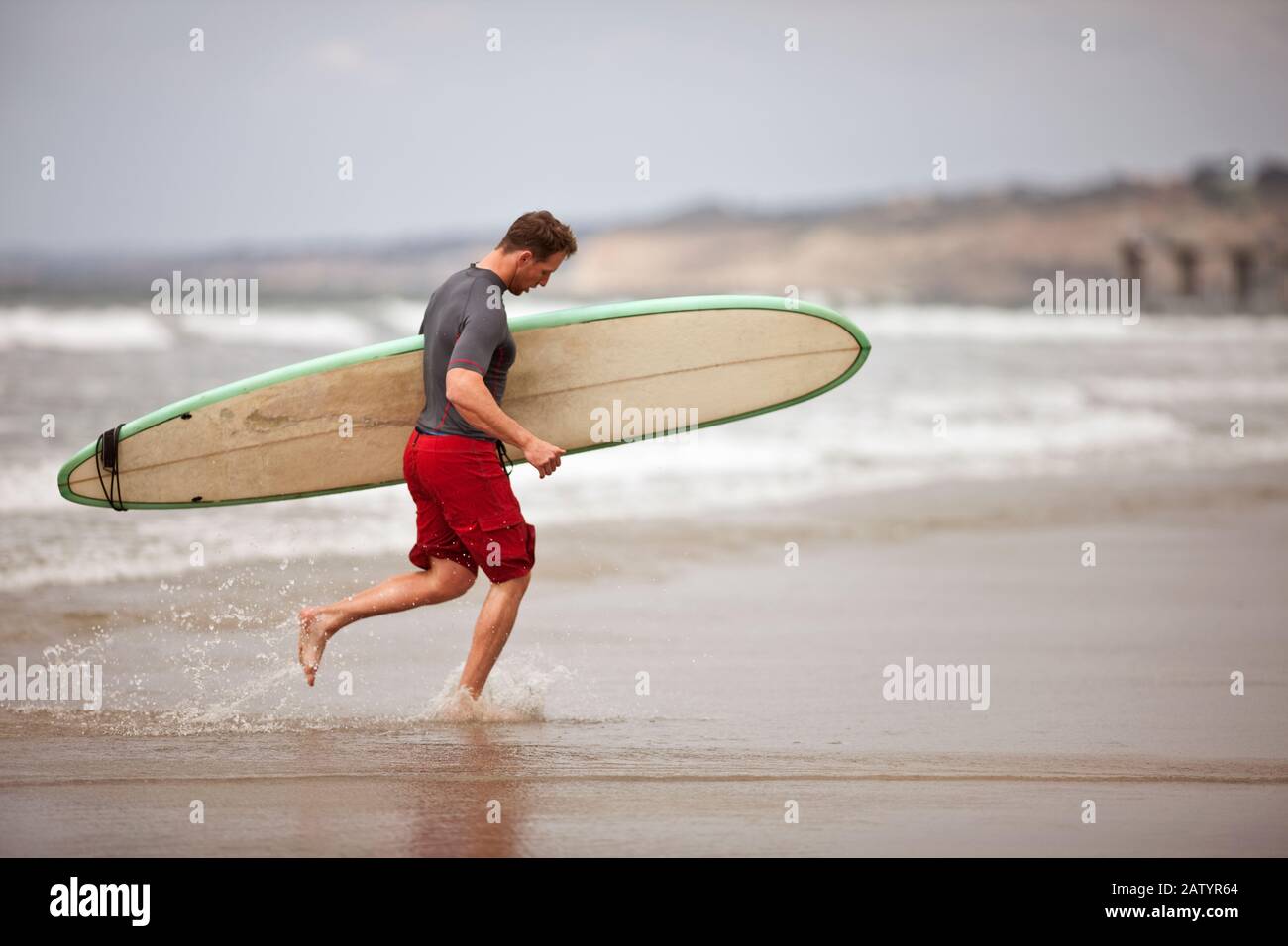 Man running out of the water with his surfboard Stock Photo - Alamy