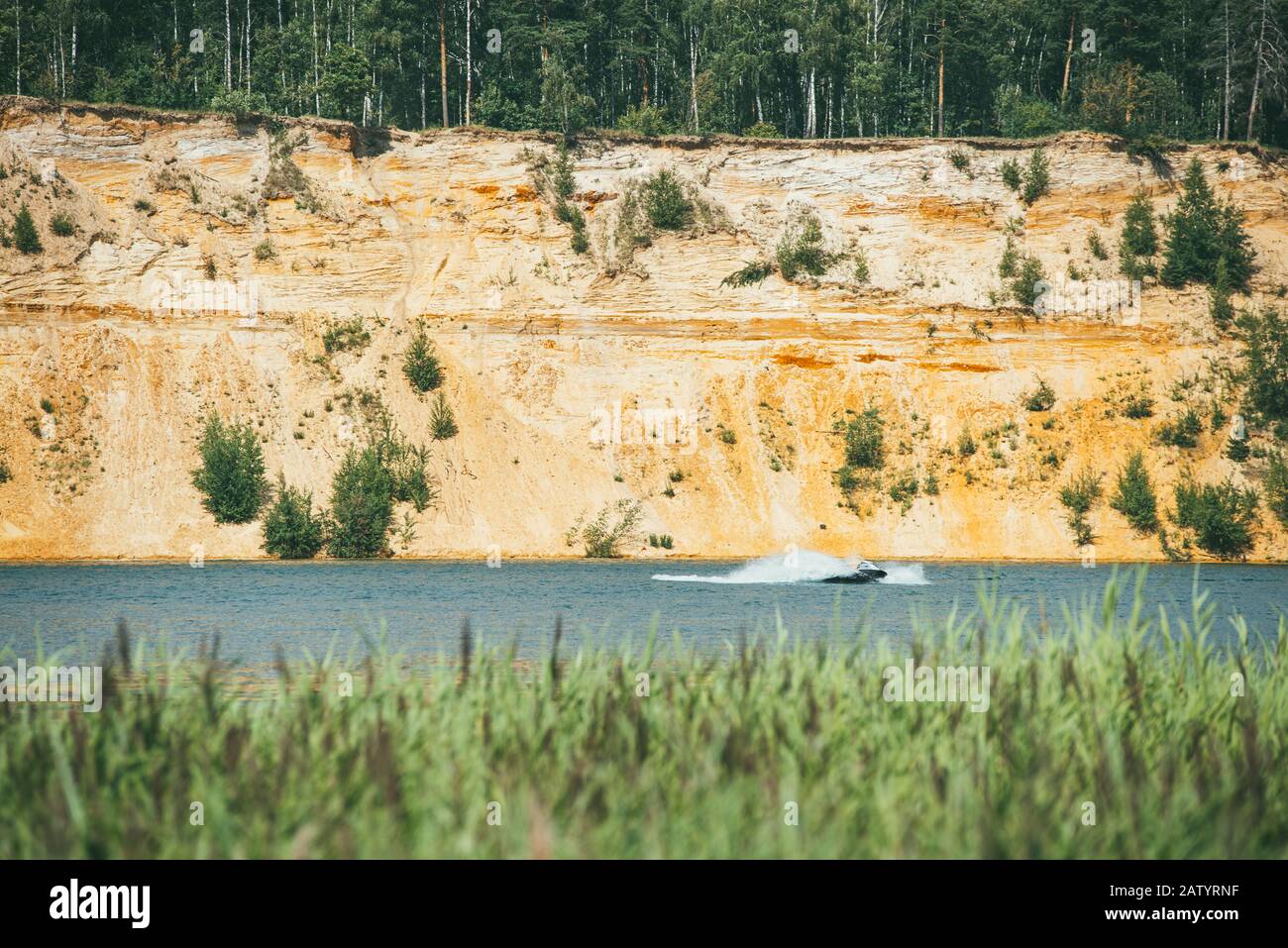 High rocky sandy steep bank covered with pine trees over a clear and ...