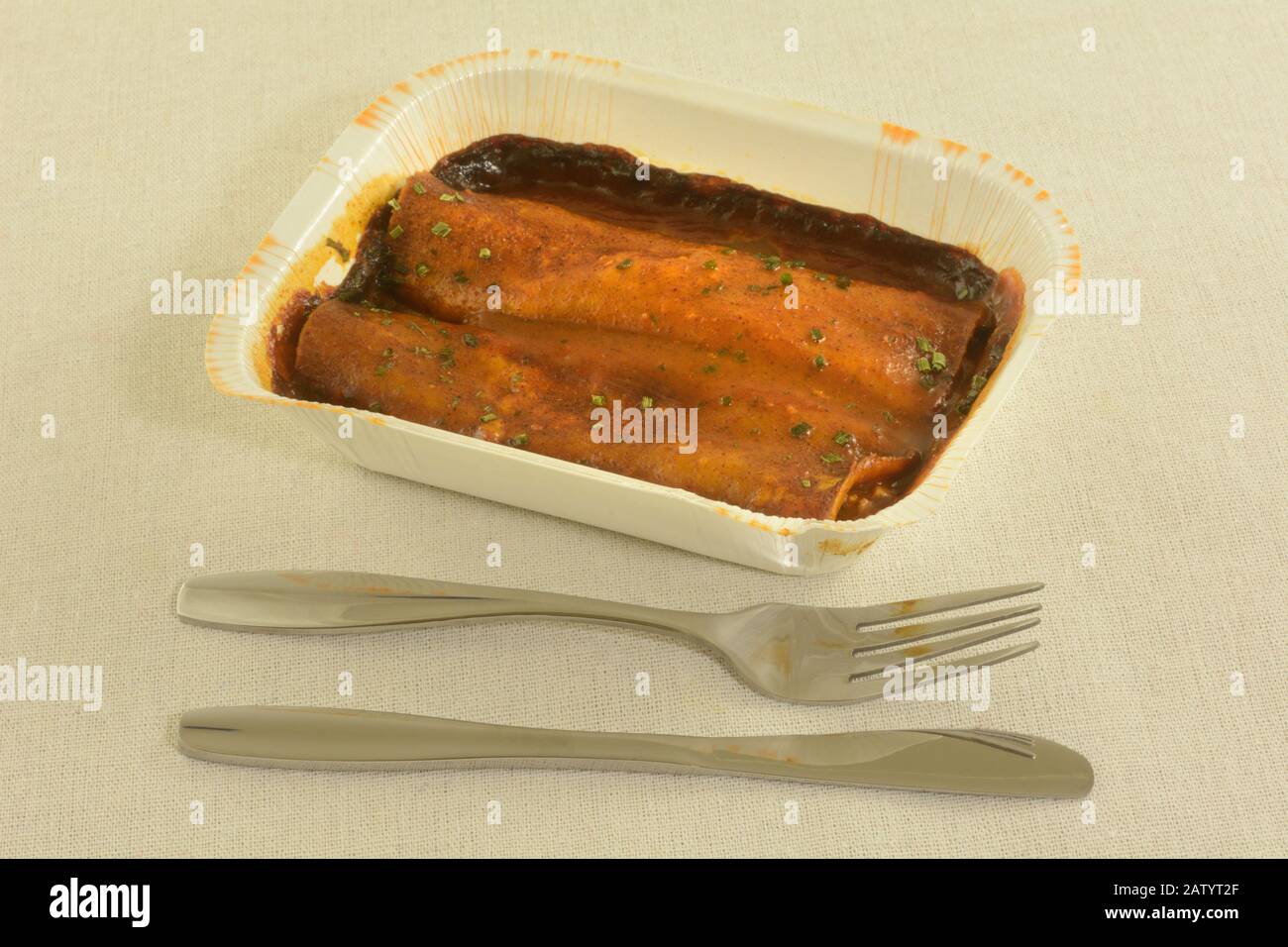 Two microwaved enchiladas in cardboard container with knife and fork ...