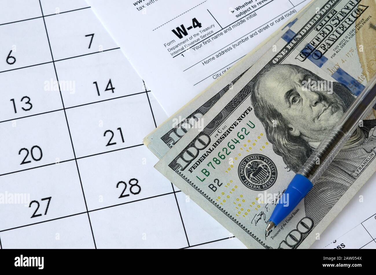 Form W-4 Employee's withholding allowance certificate and blue pen with dollar bills lies on ...