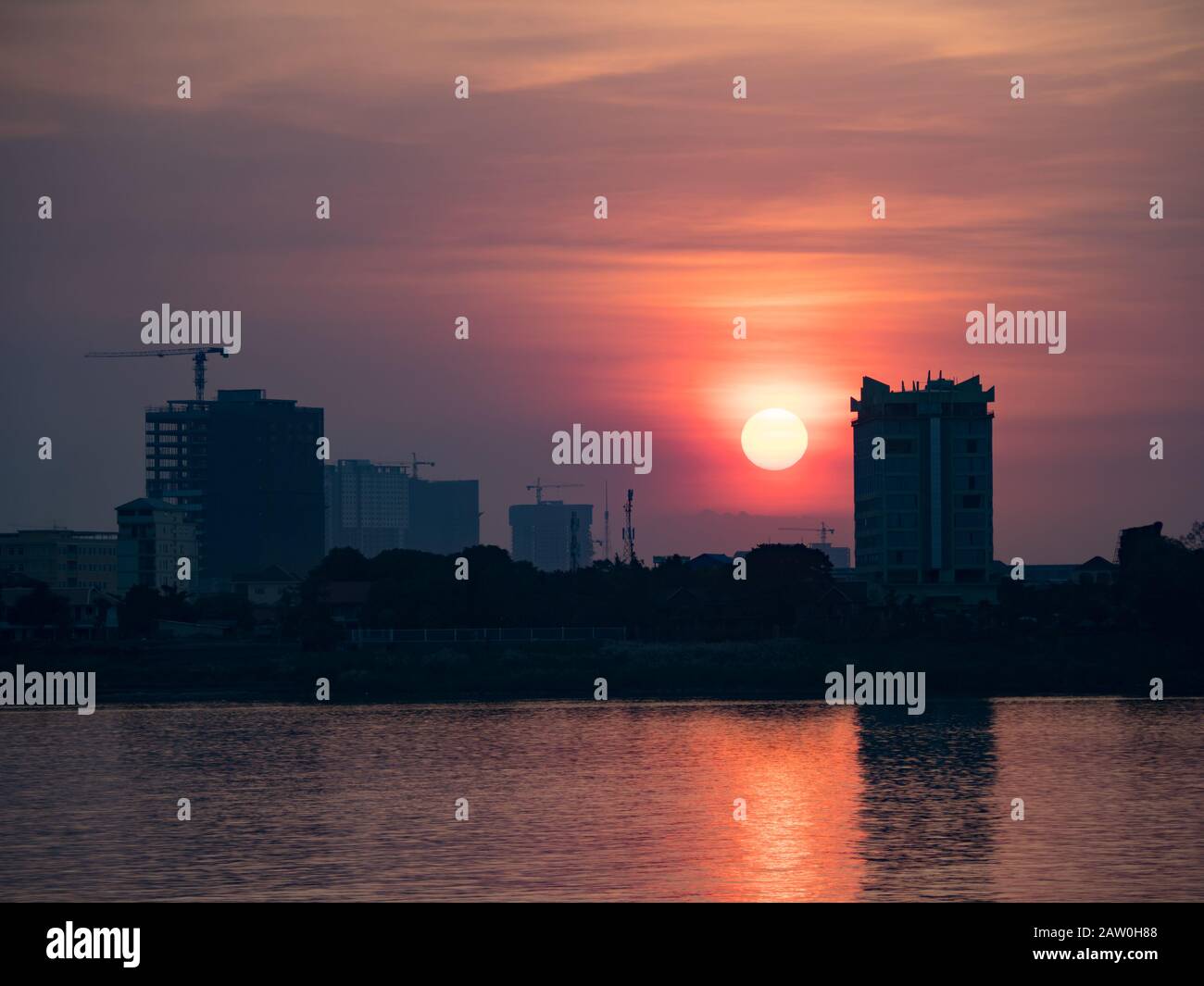 A smoggy sunset over the construction cranes of Phnom Penh, Cambodia ...