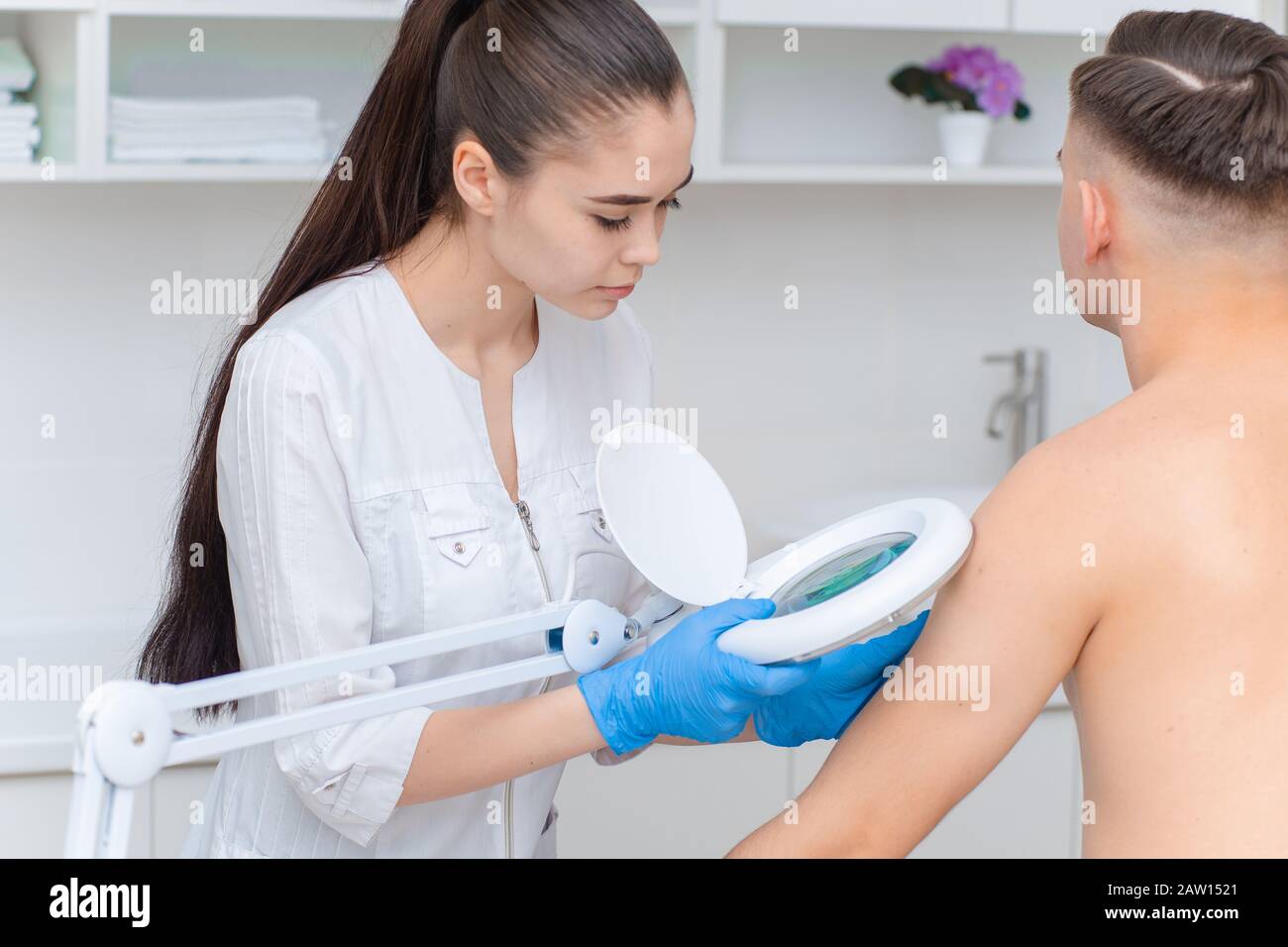 A dermatologist examines the skin on the body of a young man through a ...