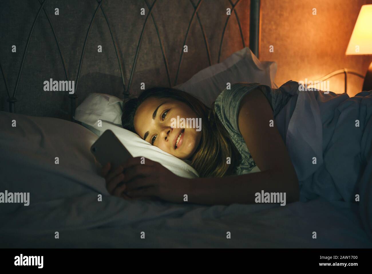 Girl uses a cell phone while lying in bed and smiling Stock Photo - Alamy