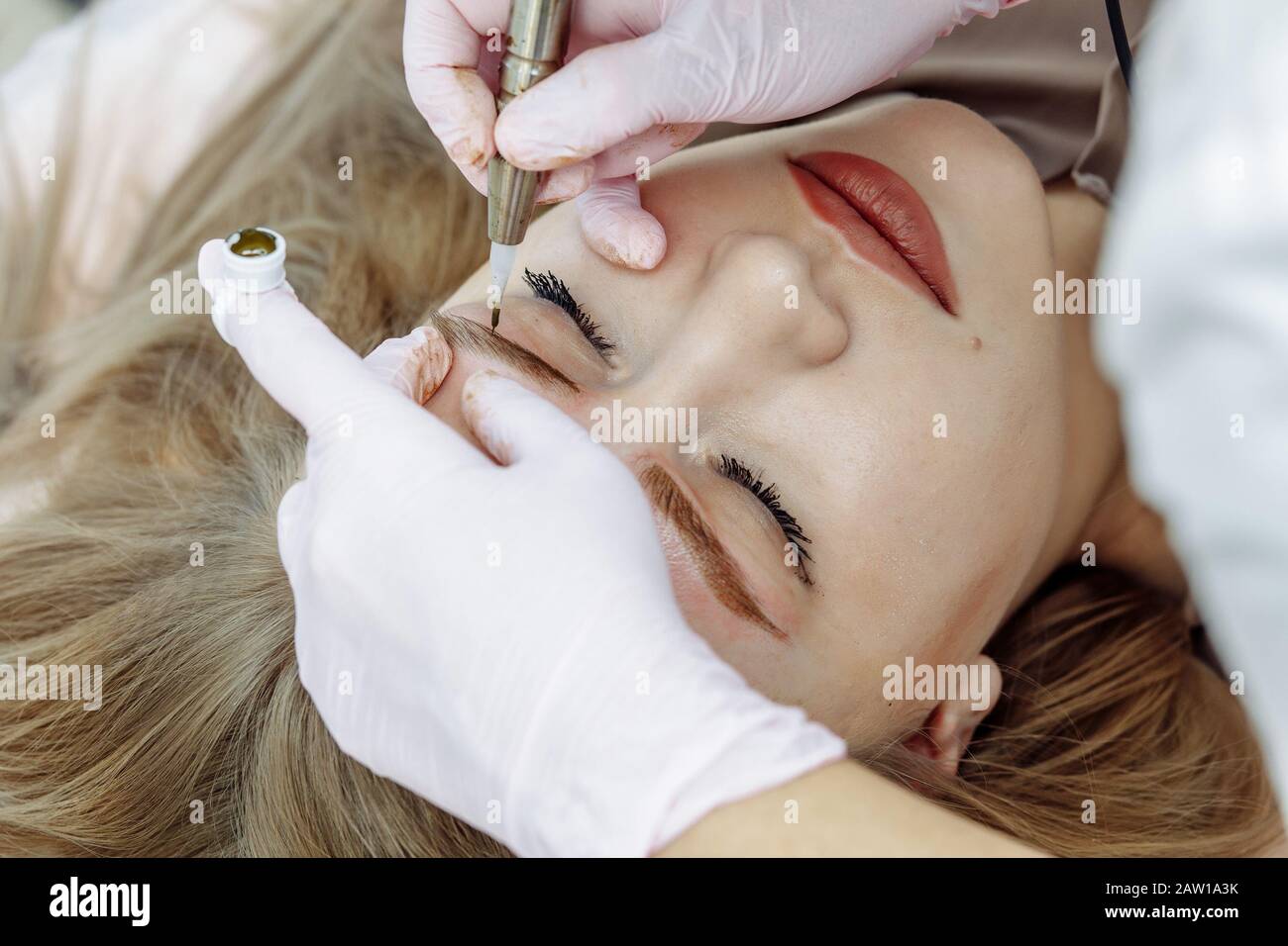 Permanent makeup, tattooing of eyebrows. Cosmetologist in white gloves ...