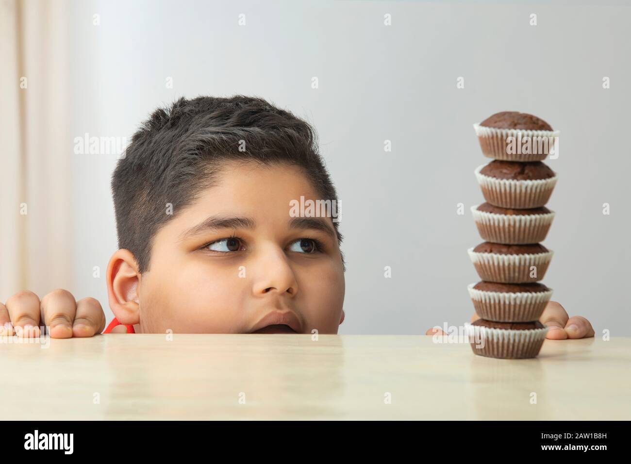 Young boy looking hungrily at cupcakes kept on the table. (Obesity ...
