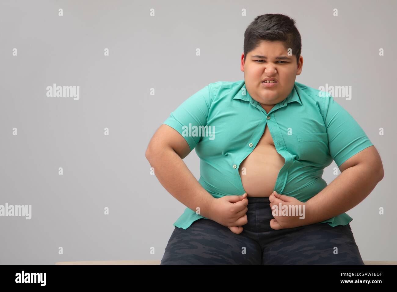 Young boy struggling to fit in a tight shirt. (Obesity Stock Photo - Alamy