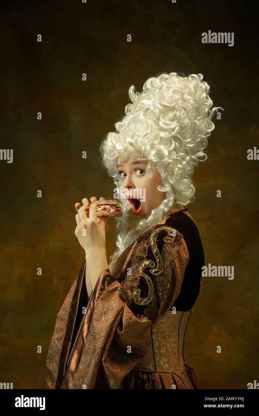 Eating burger shocked. Portrait of medieval young woman in brown ...