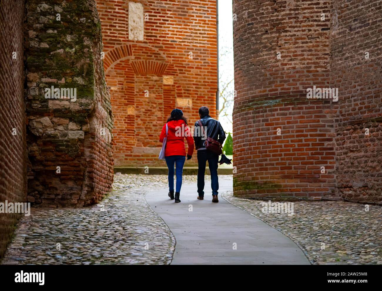 Two People Walk Between Large Brick Walls To An Opening Stock Photo - Alamy