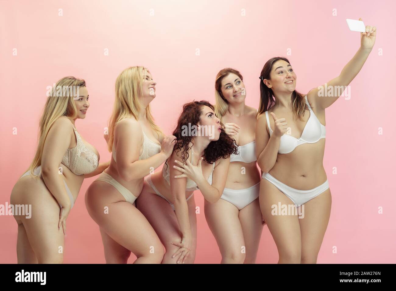 In love with myself. Portrait of beautiful plus size young women posing on pink gradient ...