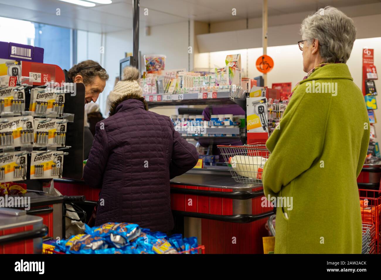 Shoppers queuing at the checkout of a supermarket putting produce on ...