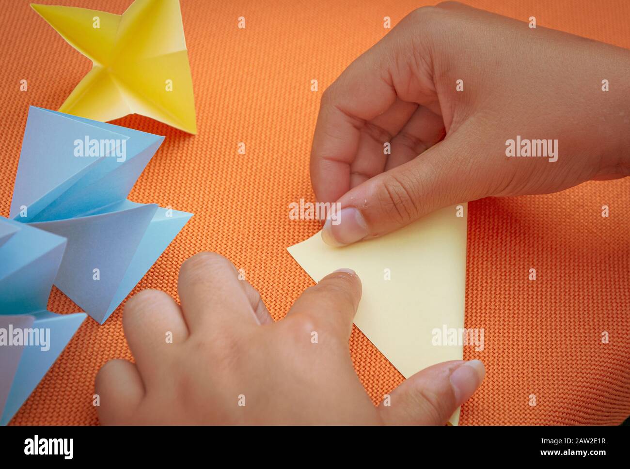 Children's hands do origami from colored paper on white background ...