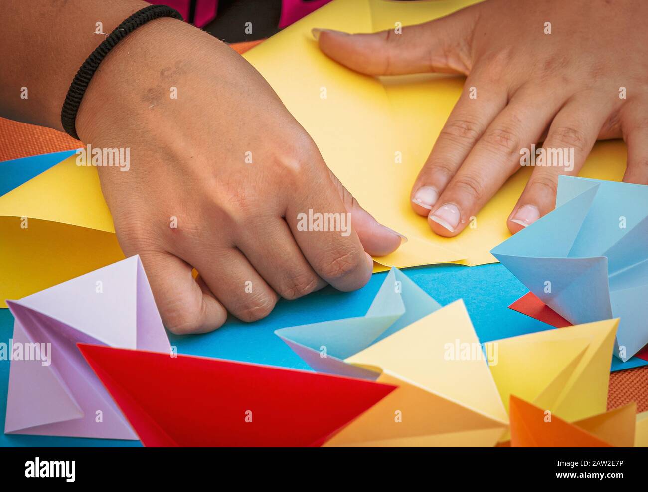 Children's hands do origami from colored paper on white background ...