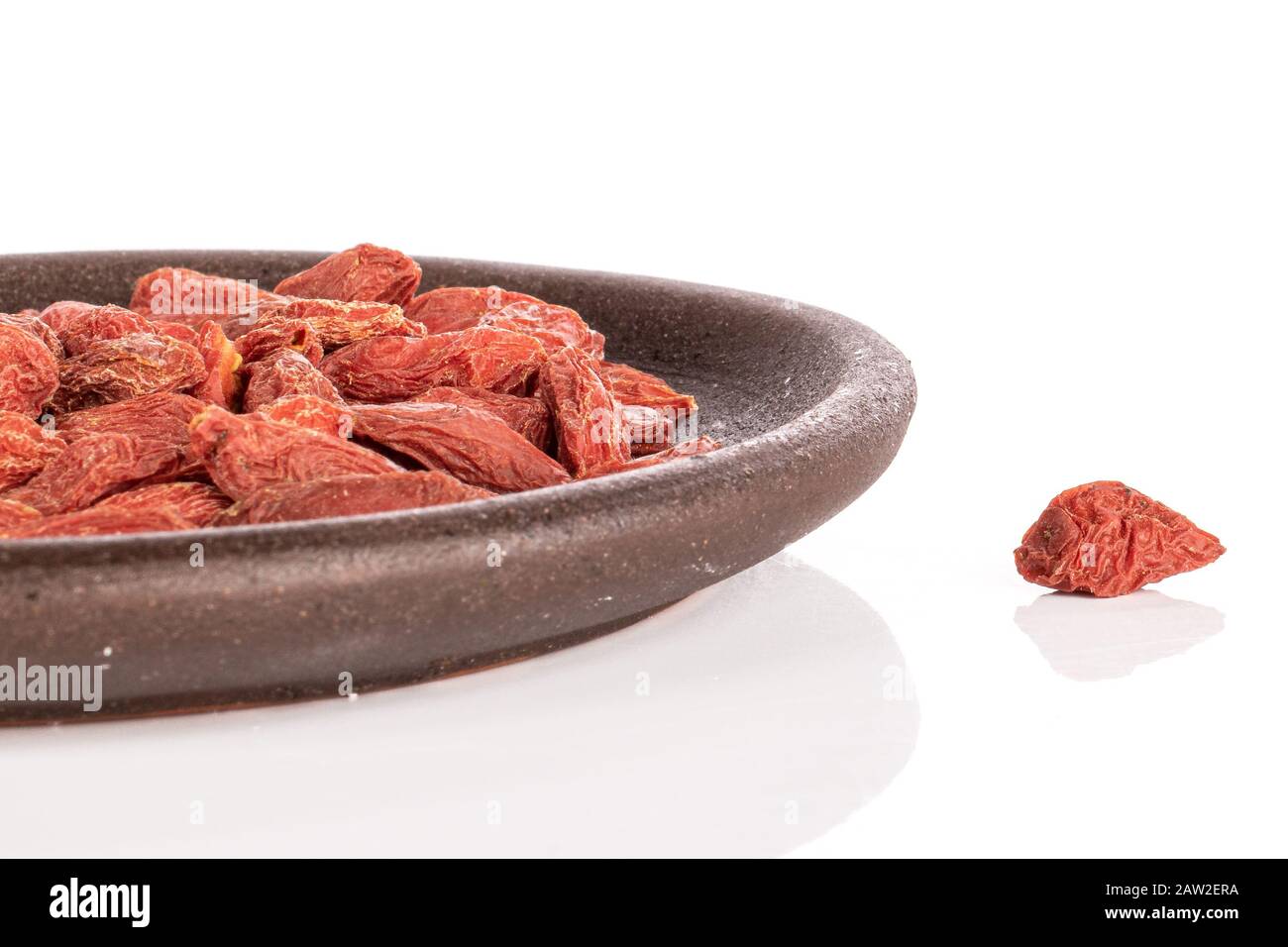 Lot of whole dried red goji with brown ceramic coaster isolated on ...