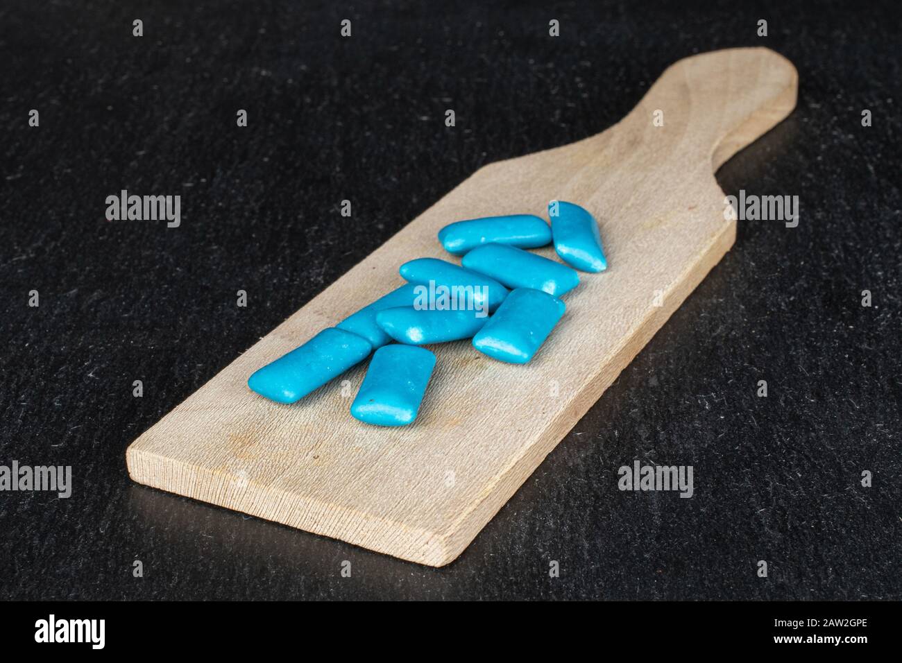 Group of nine whole blue chewing gum on wooden cutting board on grey ...