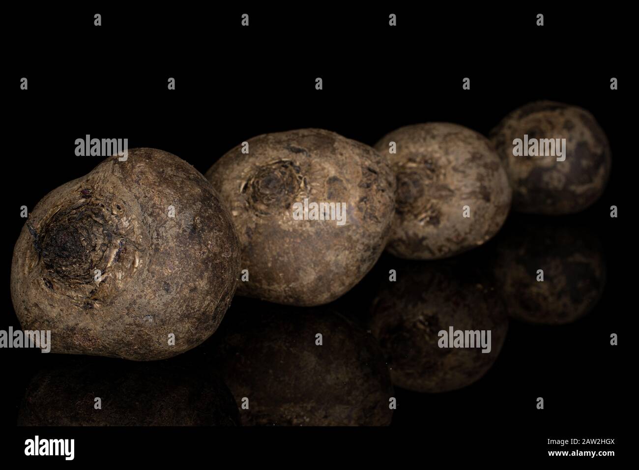 Group of four whole raw sweet beetroot diagonal isolated on black glass ...