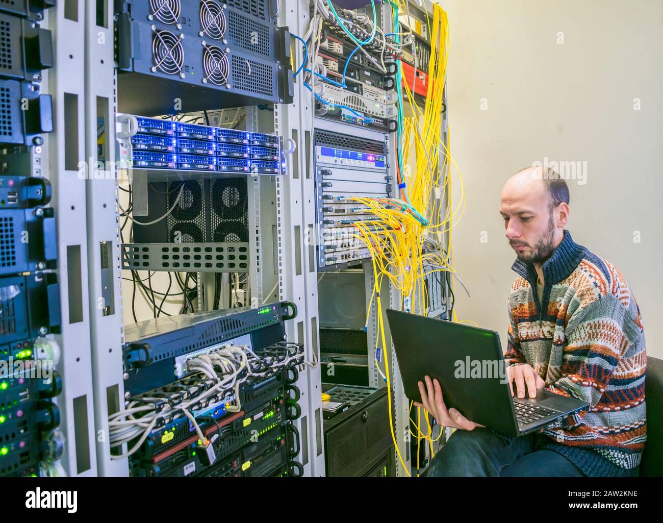 A man with a laptop sits in the server room of the data center. The ...