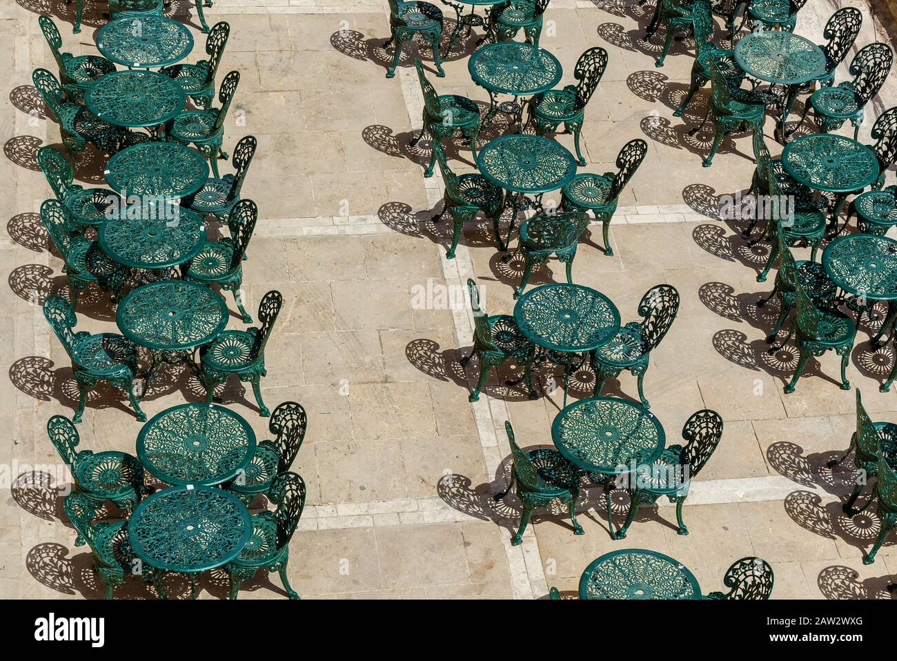 A big terrace of an open-air cafe with green metal tables and chairs ...