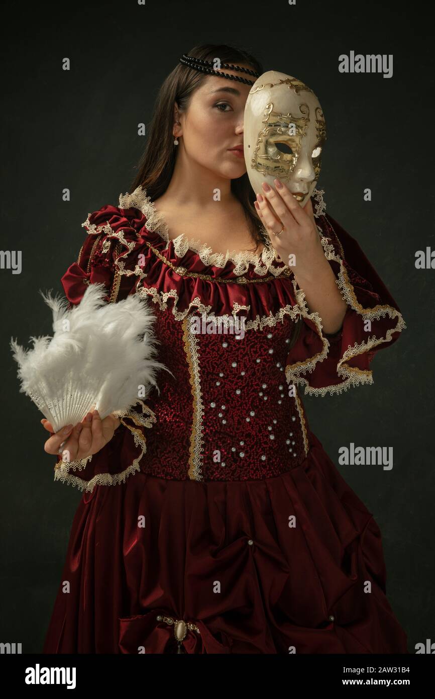 Hiding with mask. Portrait of medieval young woman in red vintage ...