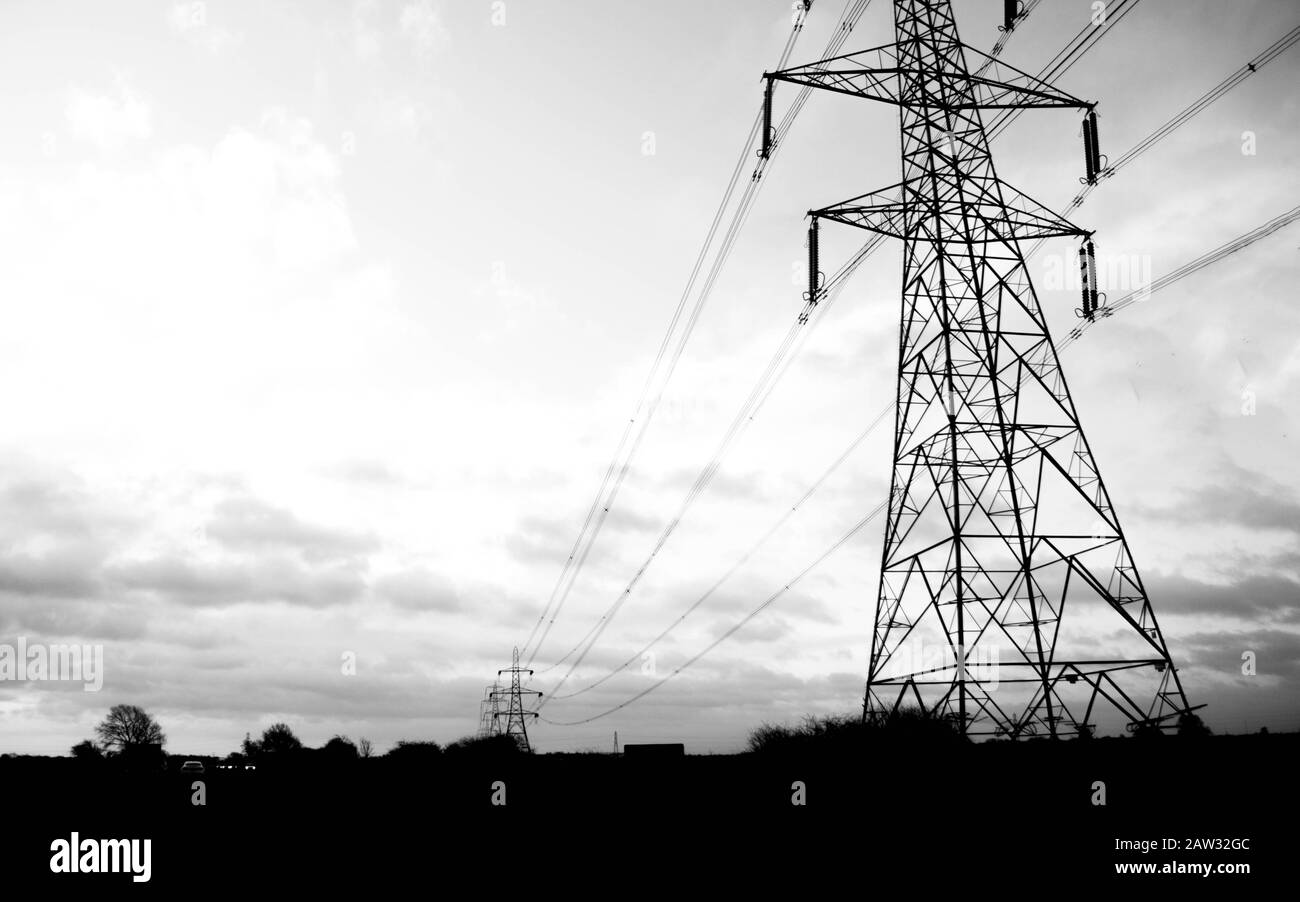 A row of electricity pylons stretch across the countryside, in the ...