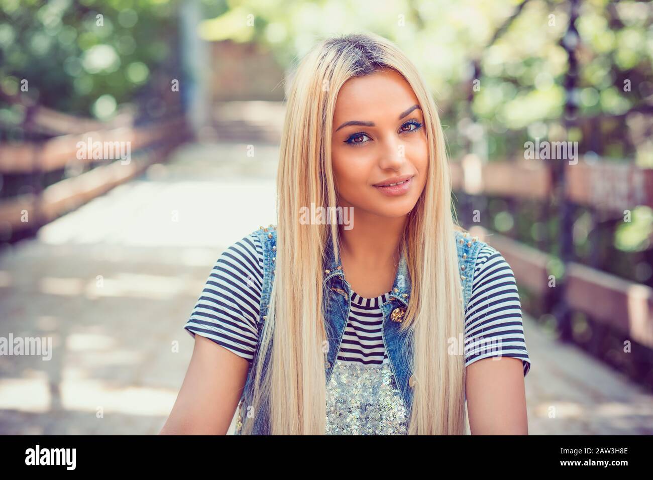 Content young model with fair hair sitting on bridge in summer park ...