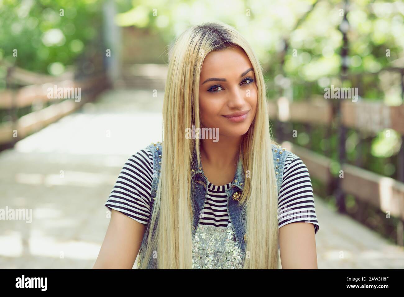 Content young model with fair hair sitting on bridge in summer park ...